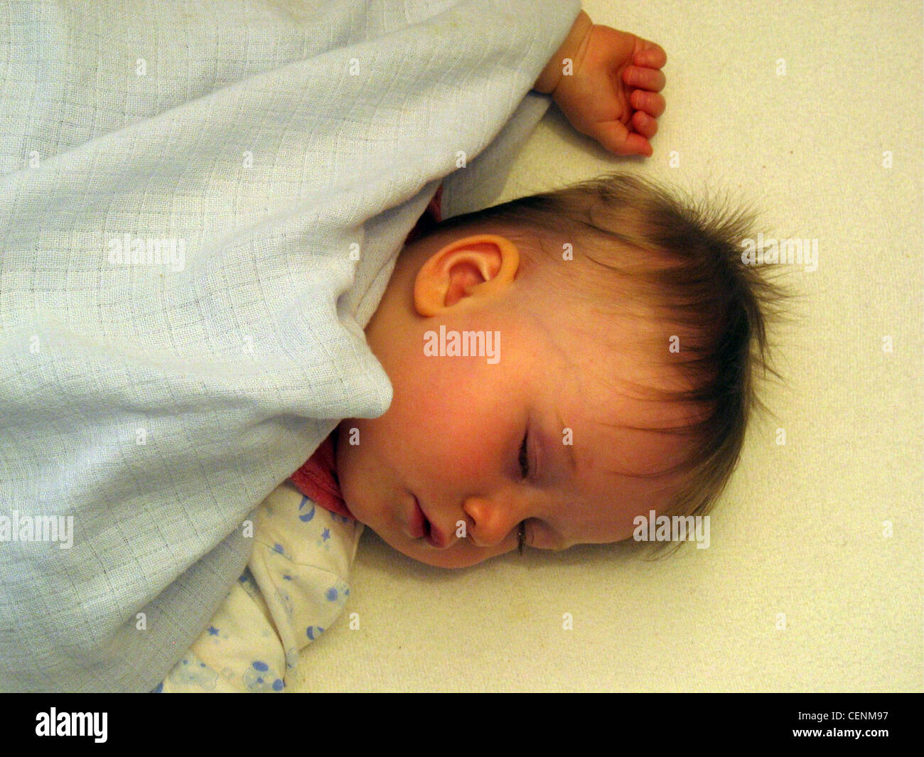 Baby with fluffy hair asleep with head turned to one side and arm ...