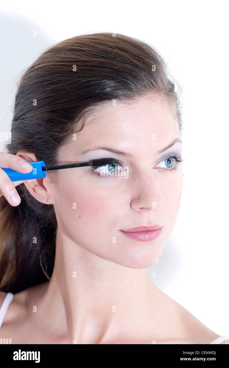 Female with brunette hair off her face, applying black mascara ...