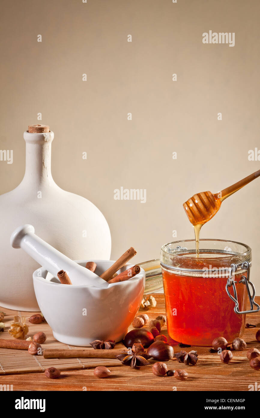 Honey dripping into a jar next to a mortar filled with cinnamon sticks ...