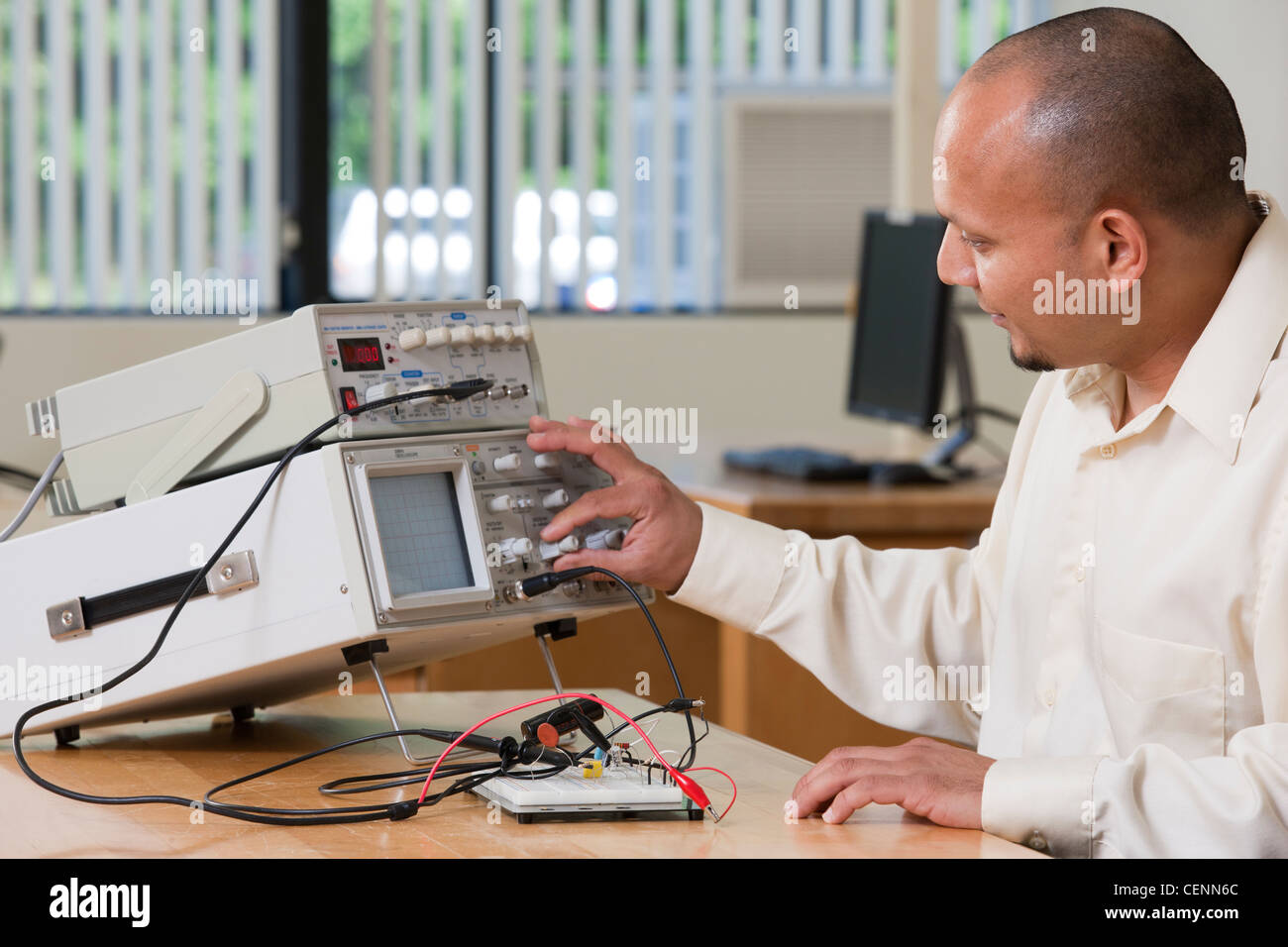 Hispanic engineering student adjusting signal levels on oscilloscope ...