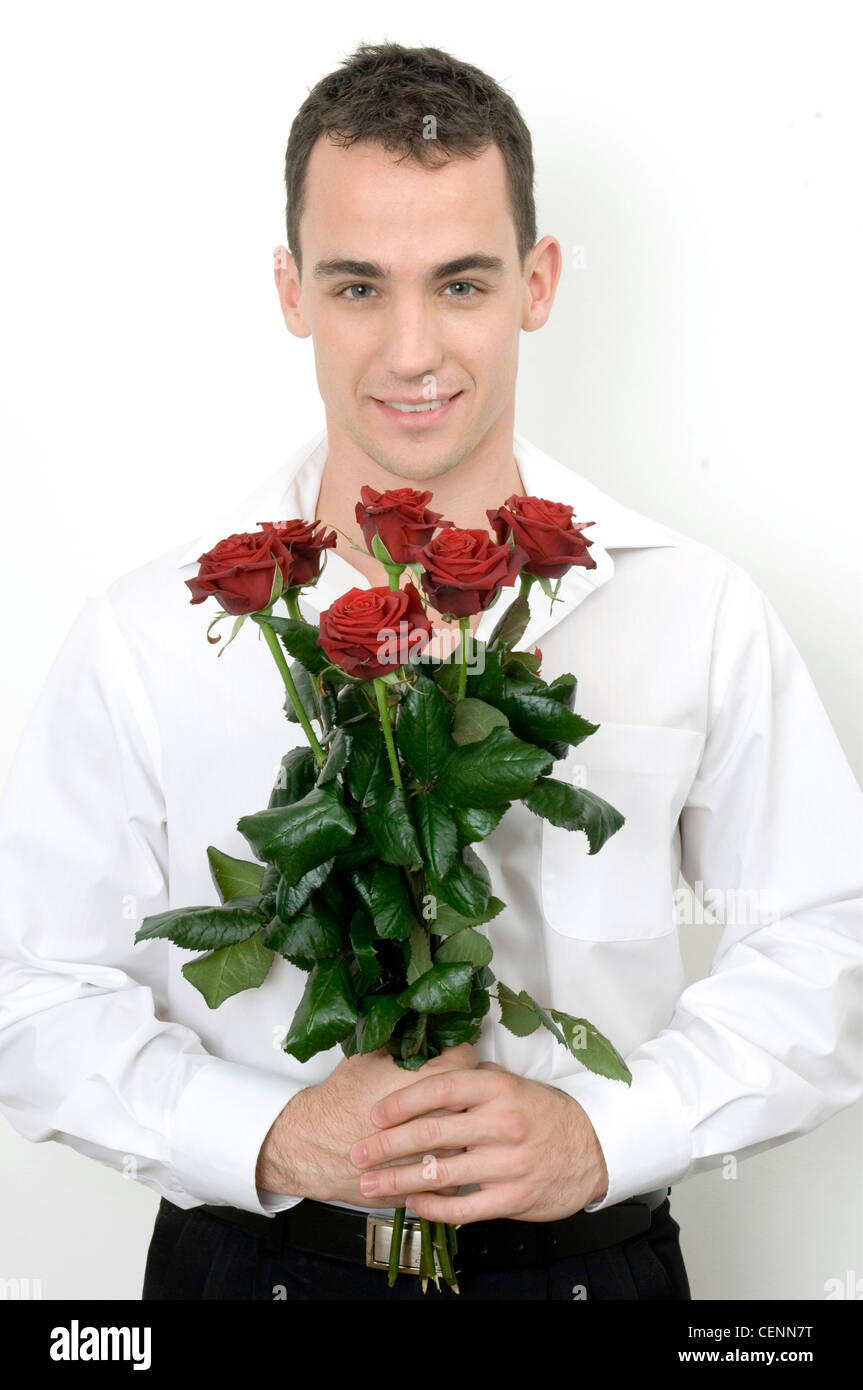 Brunette male wearing a white shirt holding a bunch of red roses ...