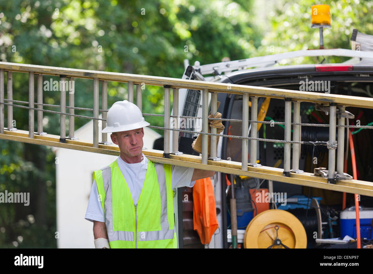 Communications worker carrying a ladder from truck to make installation ...