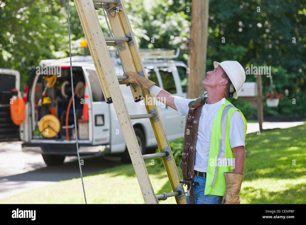 Communications worker preparing to climb ladder for overhead wiring ...
