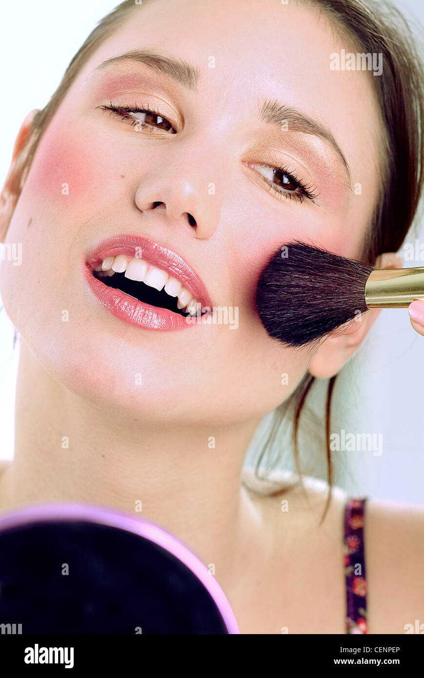 Brunette female applying pink blusher to her cheeks blusher brush ...