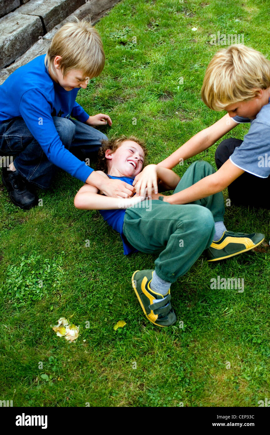 Two male children tickling another male child Stock Photo - Alamy