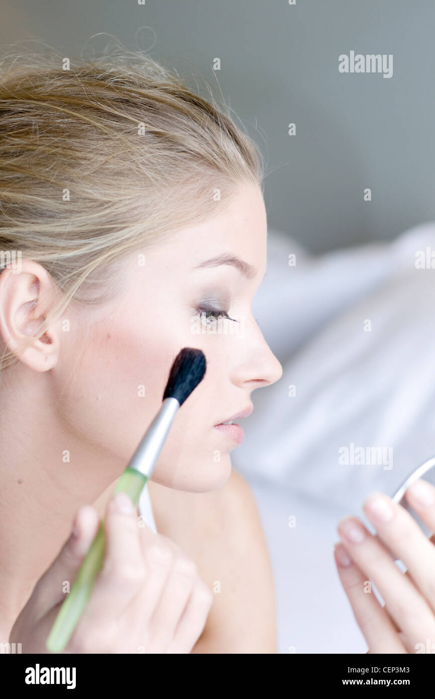 Female applying blusher to her cheek with a brush holding a compact ...