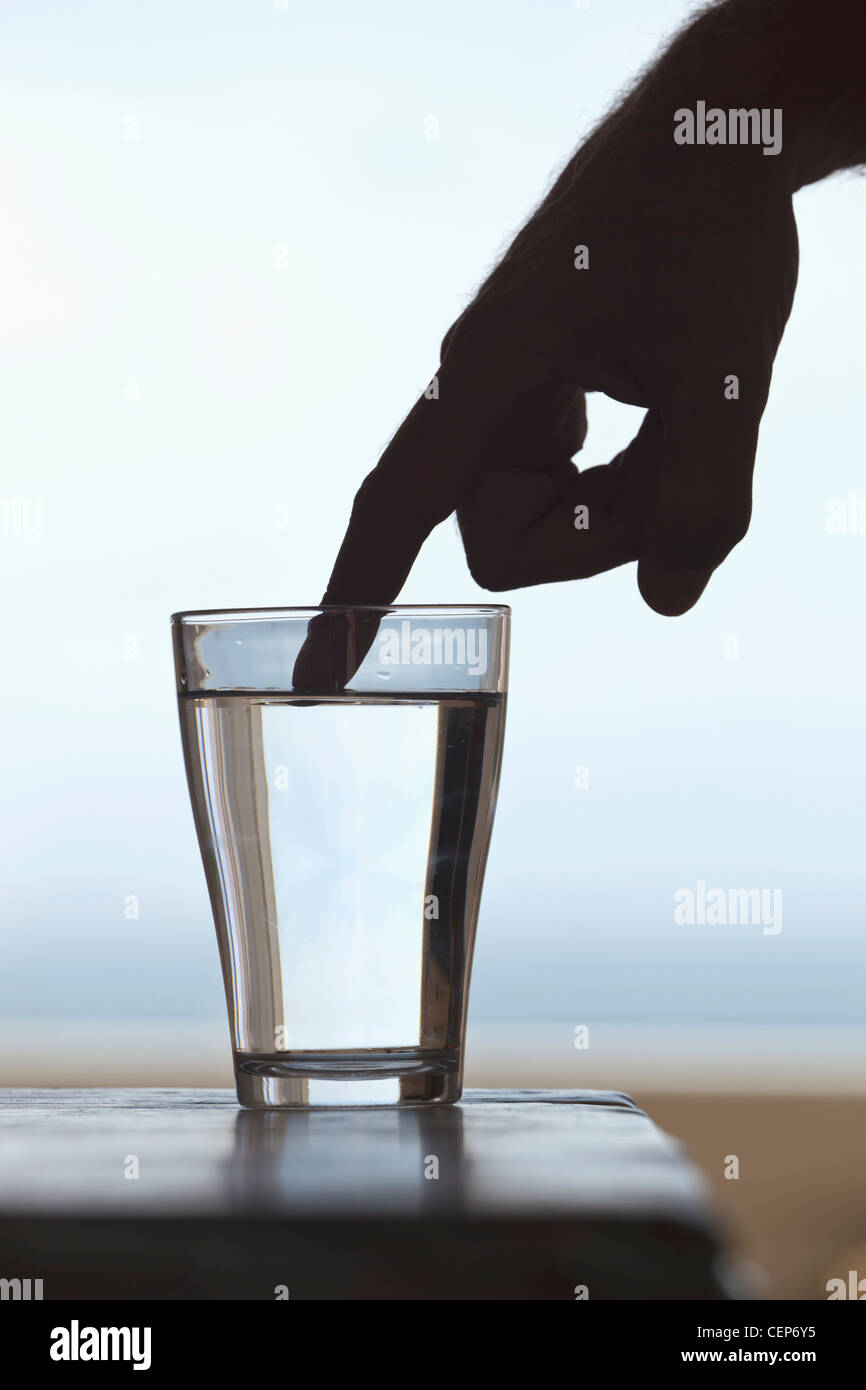 outstretched finger of silhouetted hand touching surface of water in ...