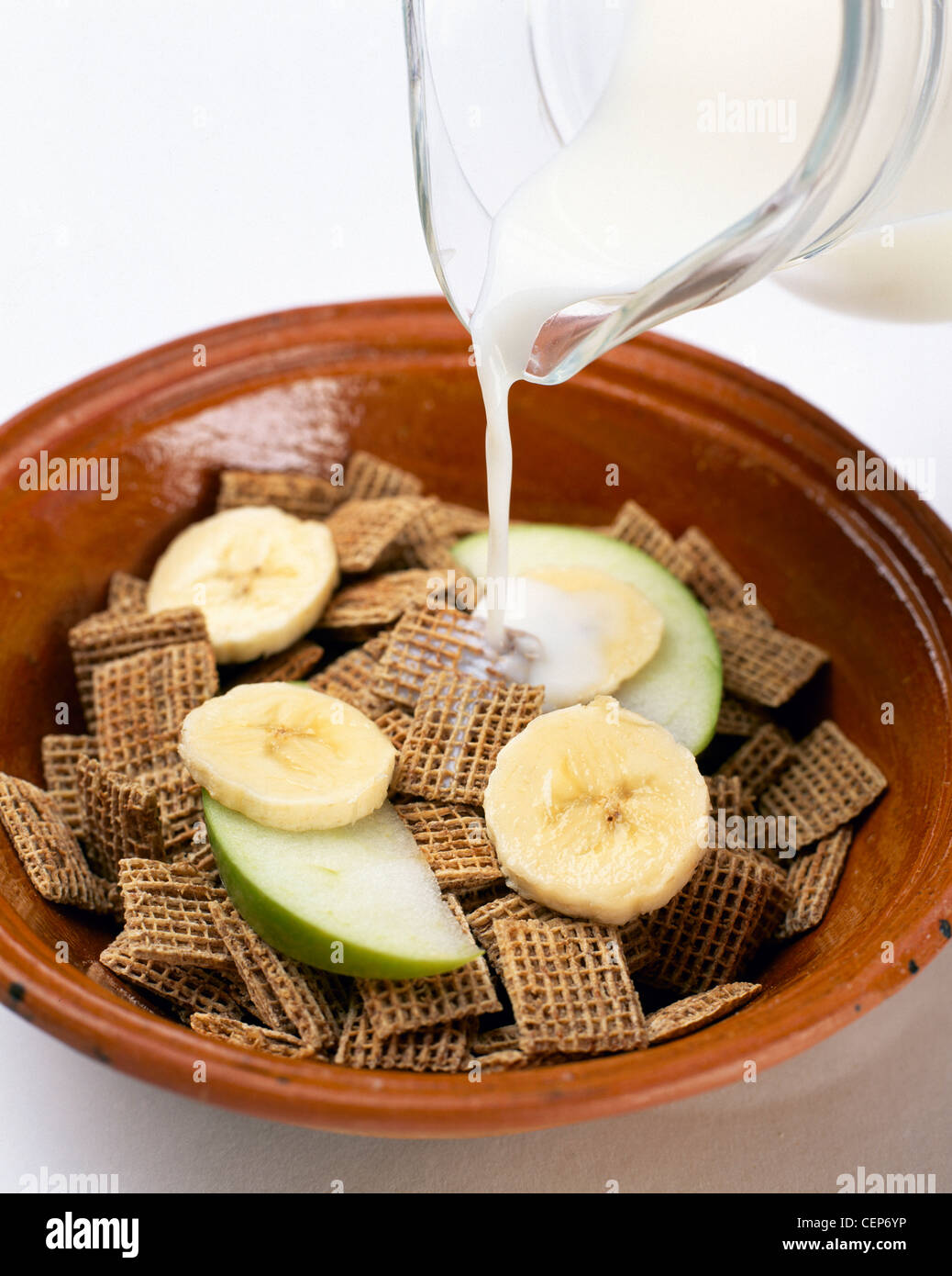 Adding milk to shreddies with sliced apple and banana in terracotta ...