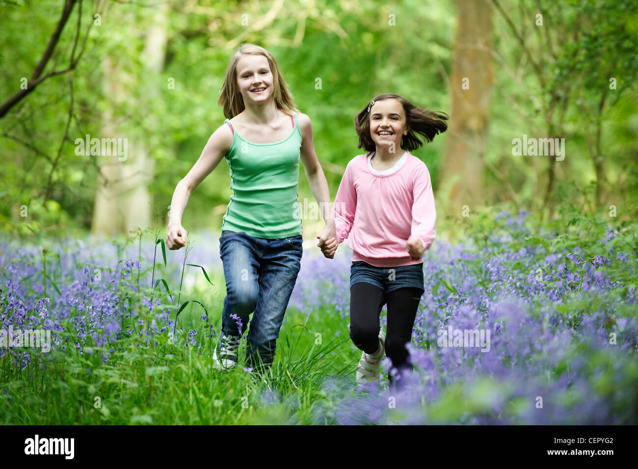 Two young girls running hand in hand through a wood full of Bluebells ...