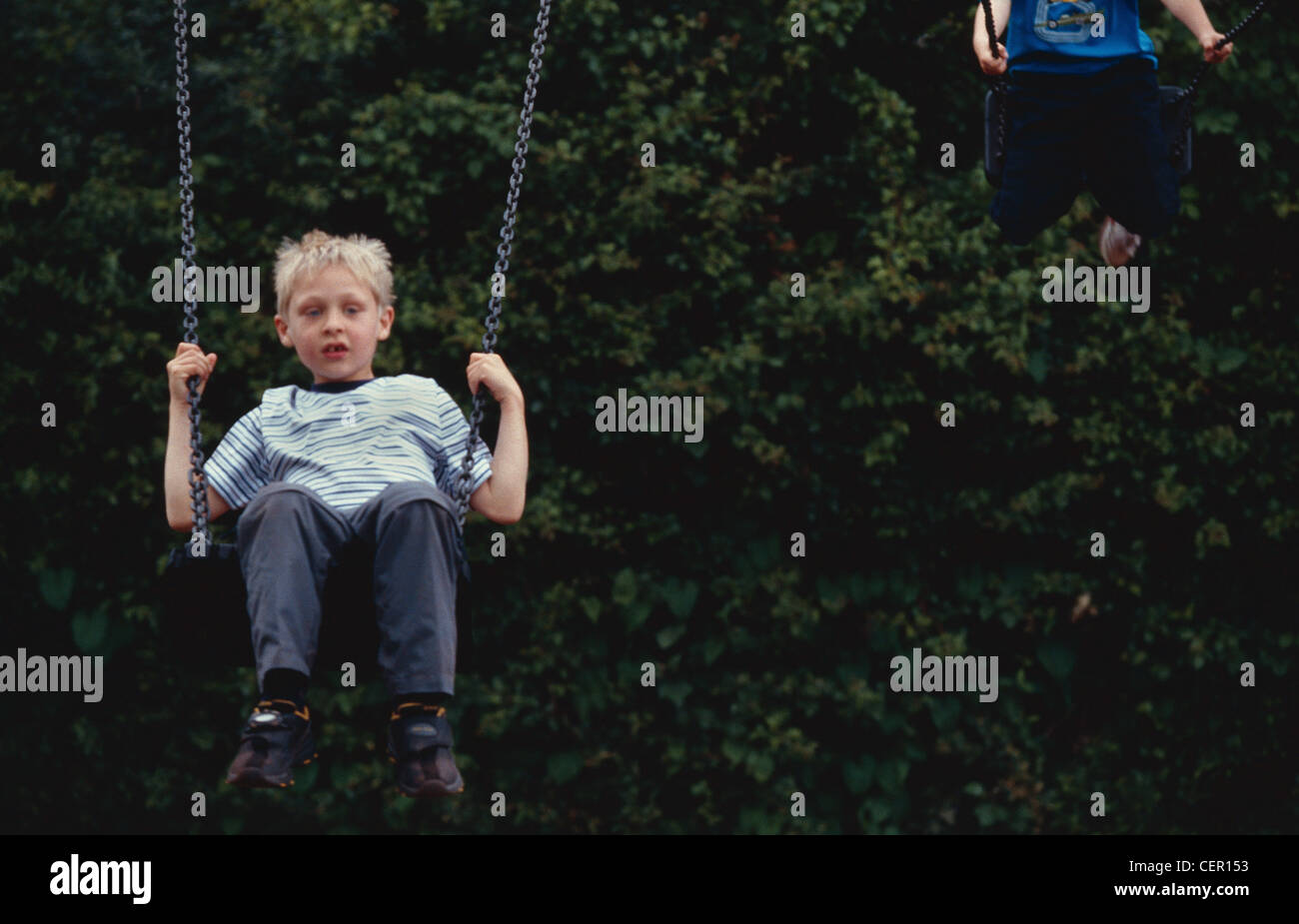 Male child with blonde hair mid air on swing looking concerned other ...
