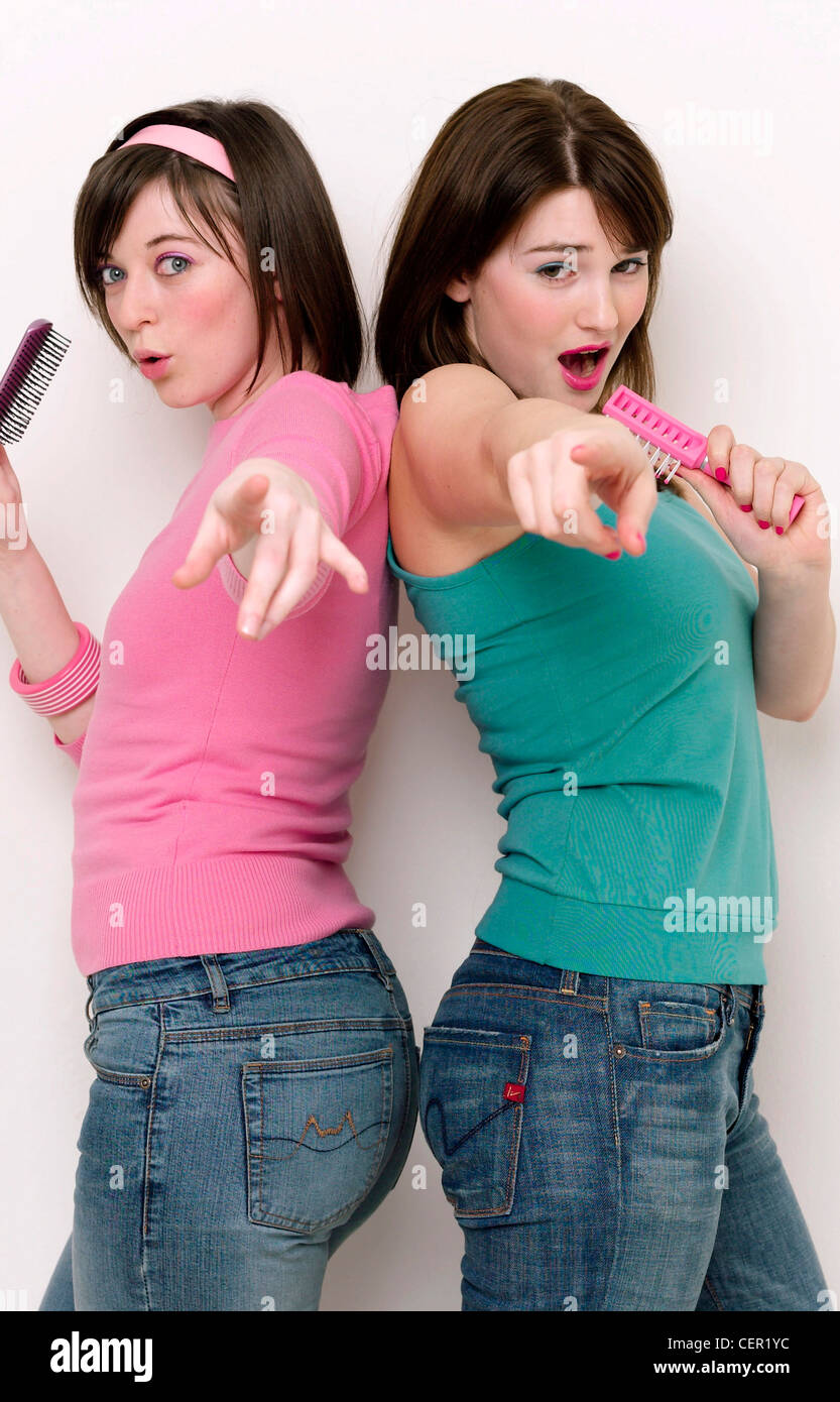 Two female teenagers back to back singing into hair brushes, female on ...
