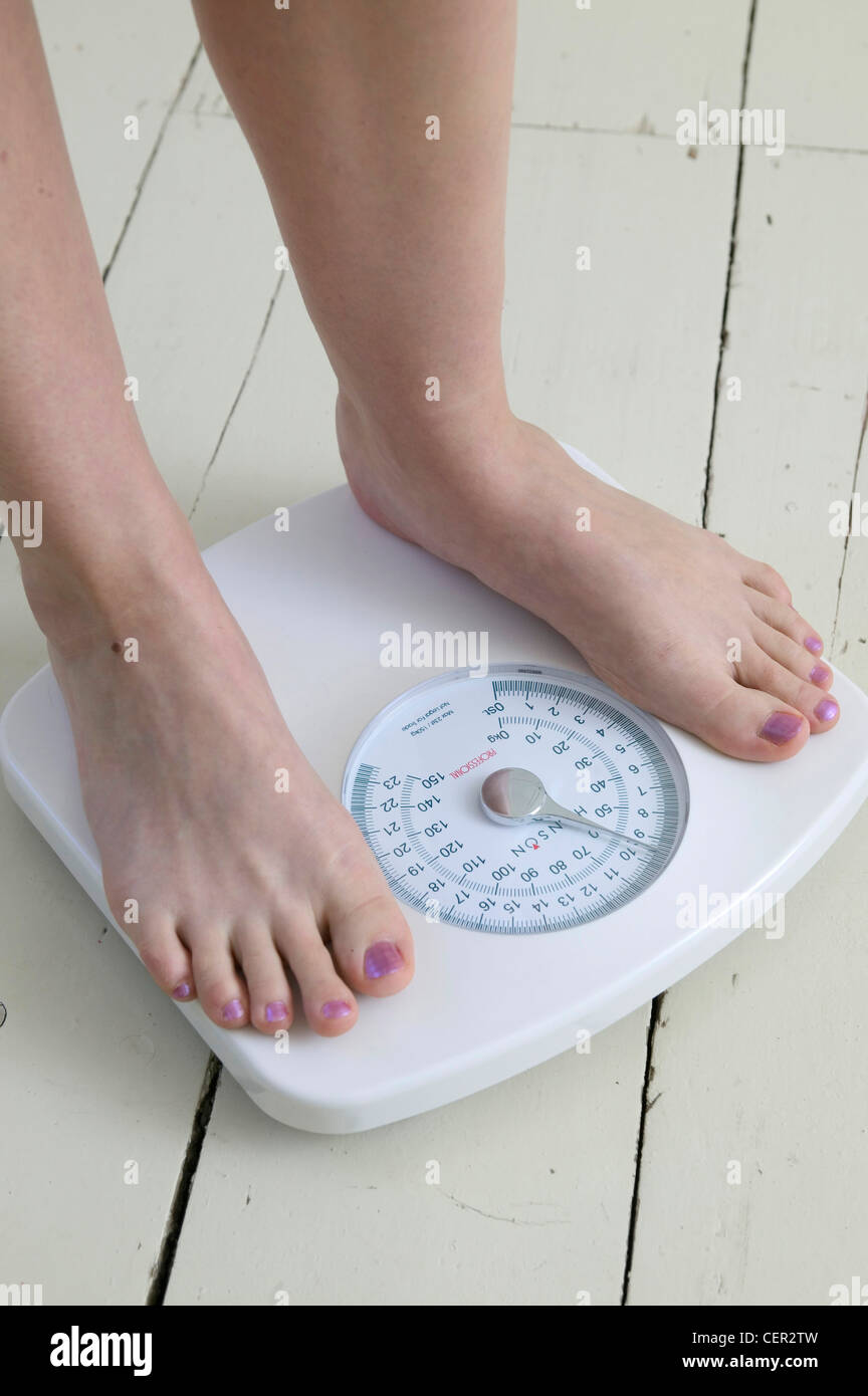 Cropped feet of female standing on white bathroom scales on white wood ...