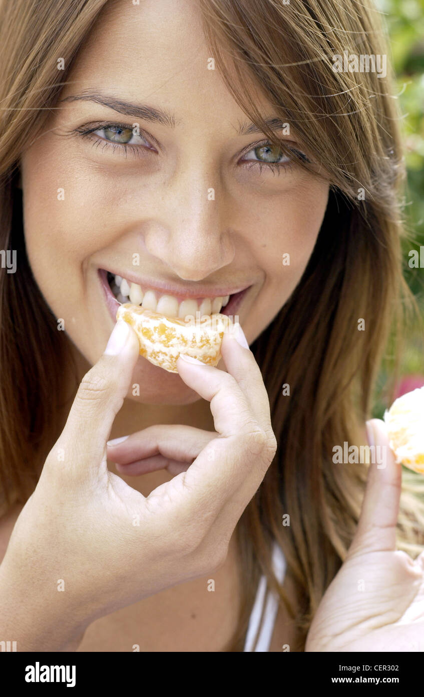 Close up of female long brunette hair, biting into orange segment ...