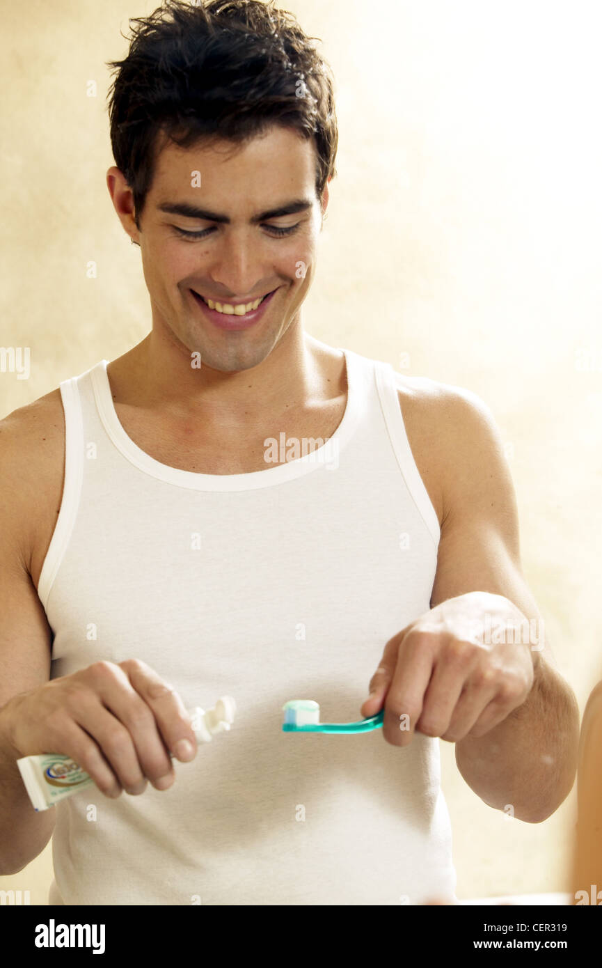 Male dark brown hair wearing white vest top, putting toothpaste from ...