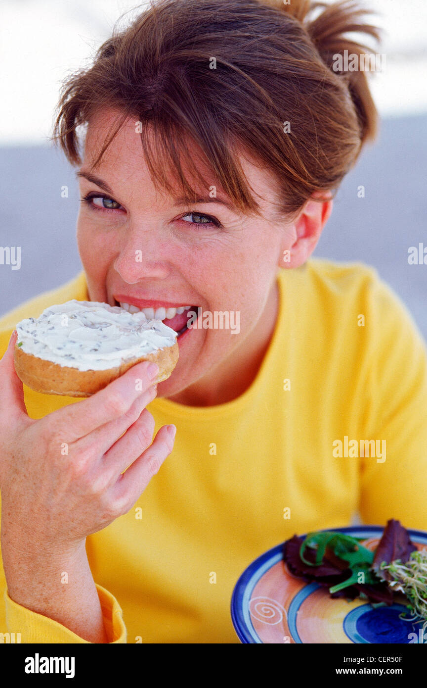 Female brunette hair off face wearing yellow t shirt eating bagel ...