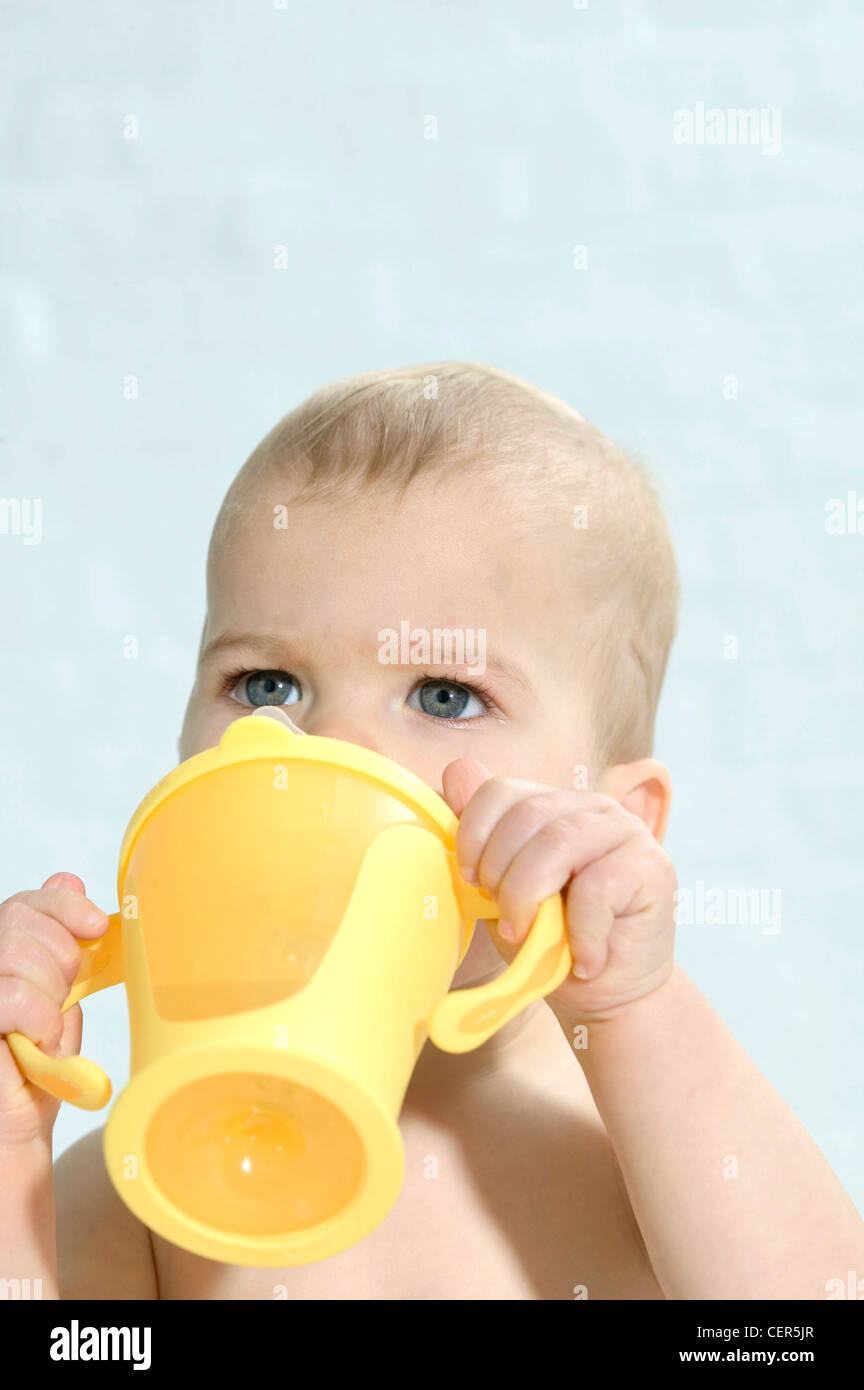 Close up of male baby drinking from yellow plastic beaker, looking up ...