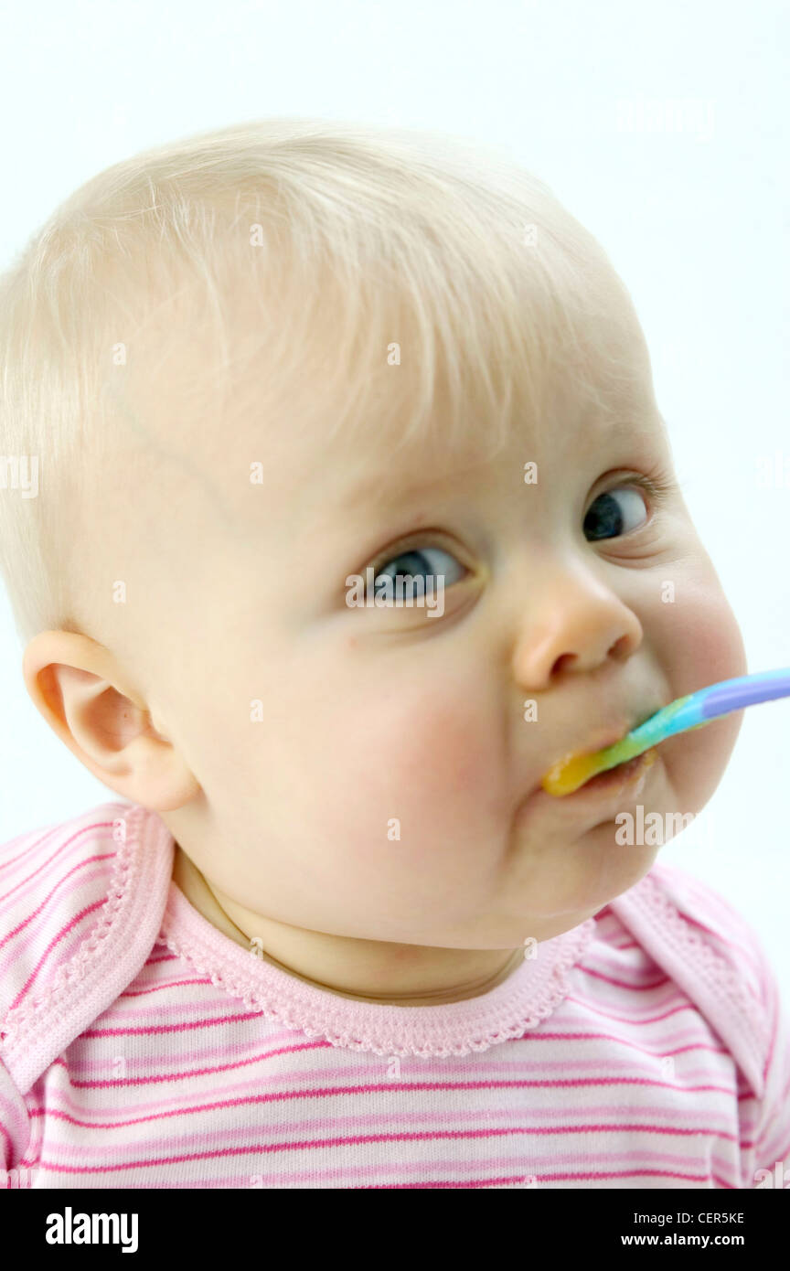 Female baby wearing pink striped babygro, being fed from plastic spoon ...