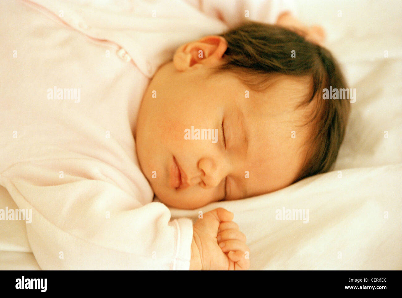 Baby with dark brown hair in pink babygro lying on back with face ...