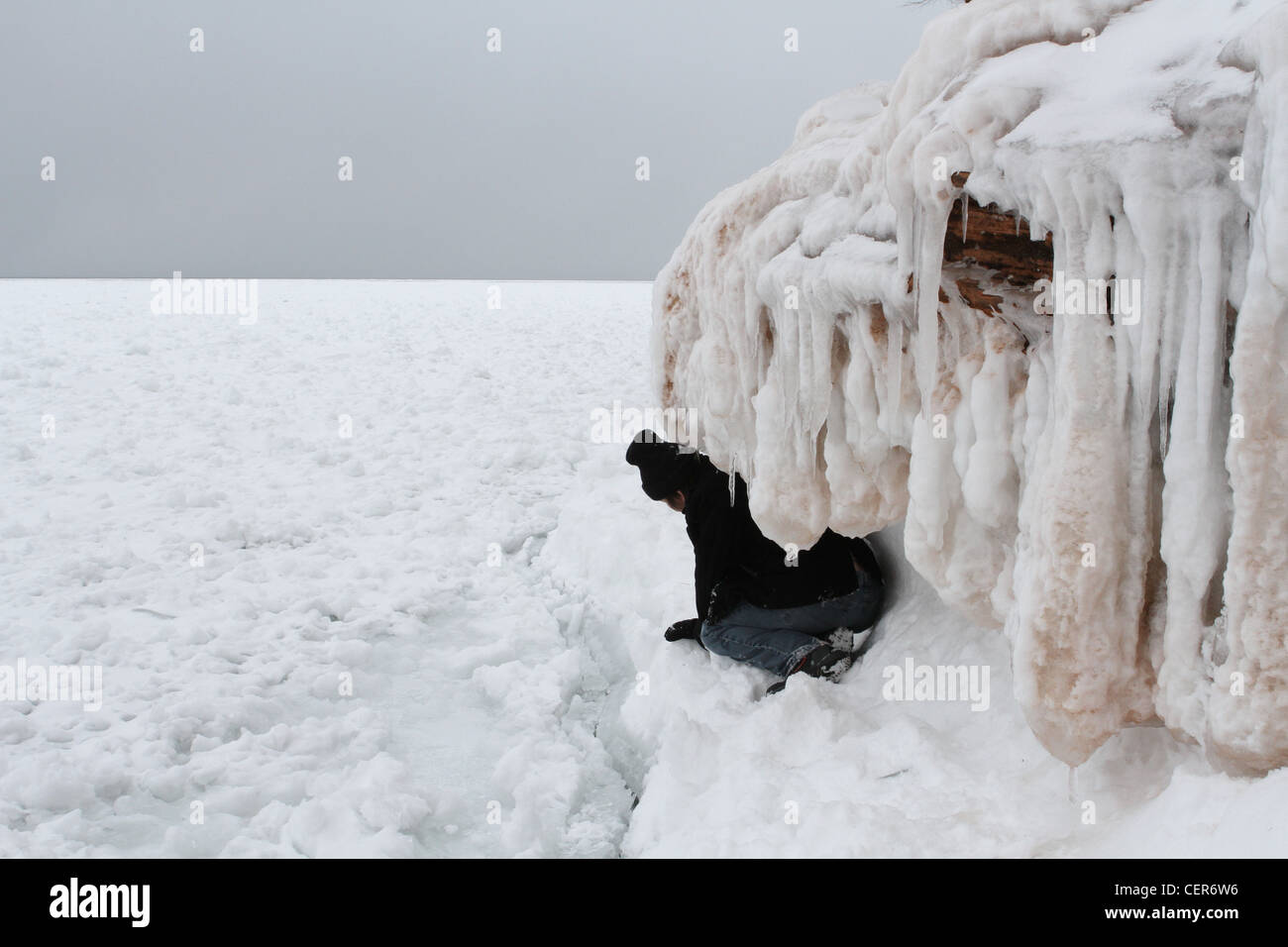 A man on hands and knees crawling on an ice ledge near the ice caves of ...