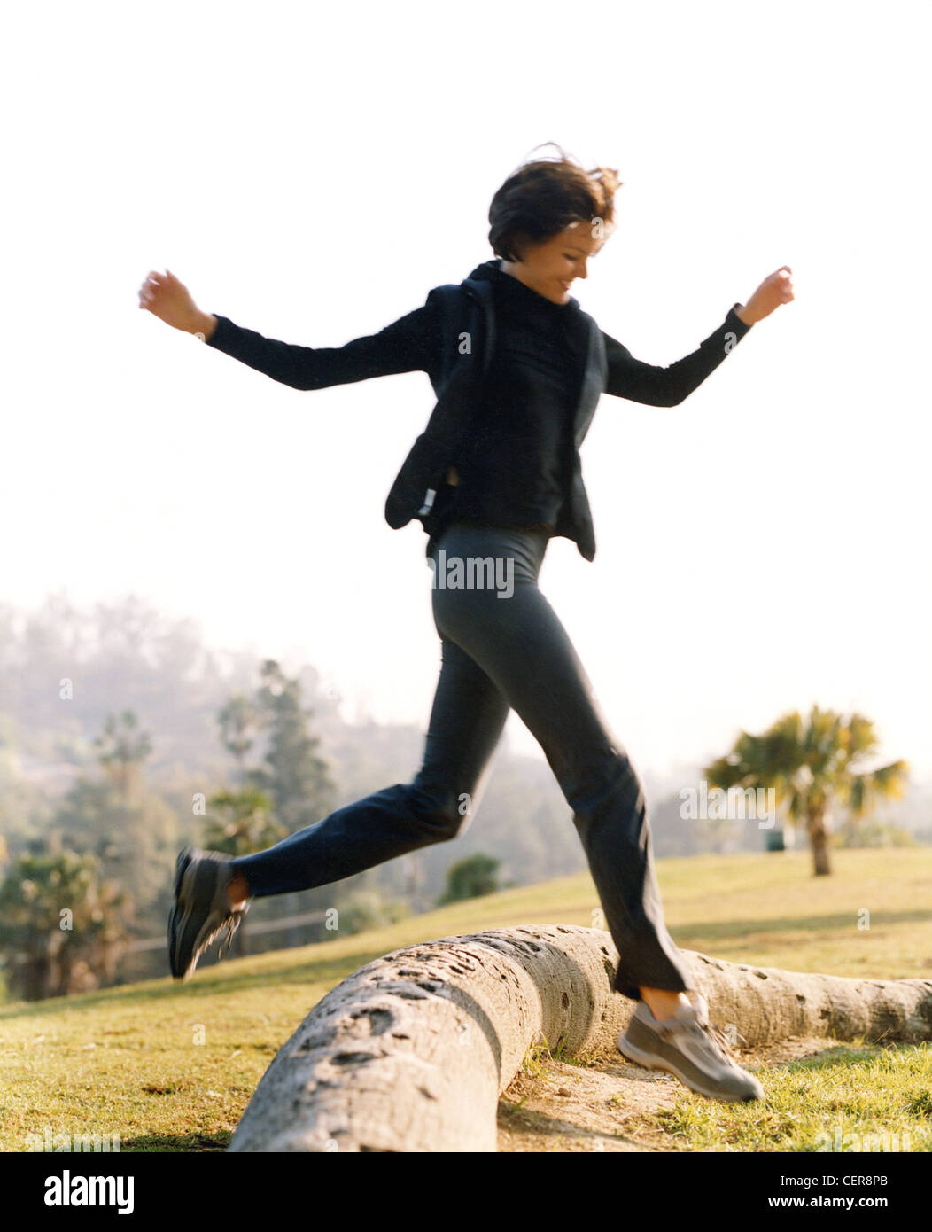 Smiling female short hair jumping over a log in a field She is wearing ...