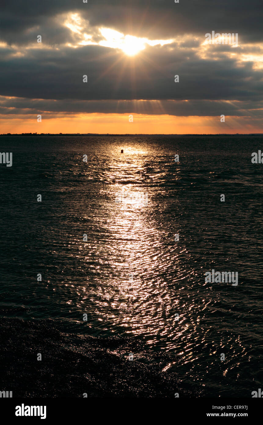 Sunlight bursting through dark clouds glinting on the water of the ...