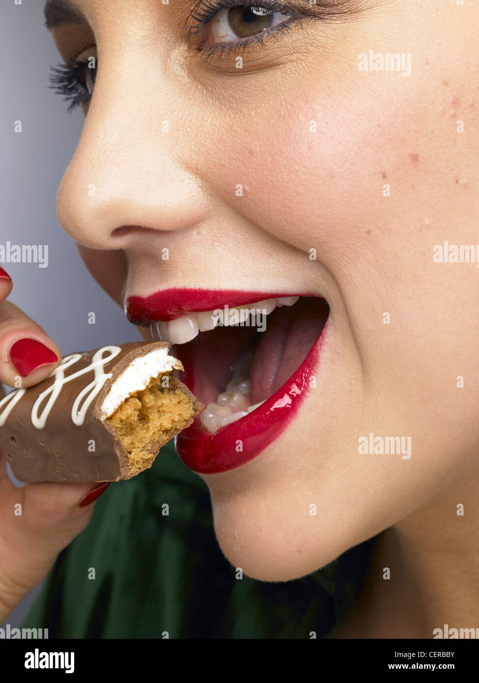 Brunette female wearing glossy red lipstick biting a chocolate covered ...