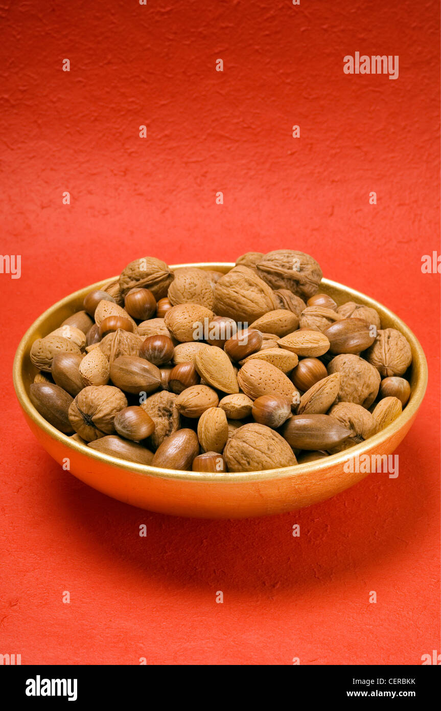 A gold bowl of mixed nuts in their shells, including almonds, hazelnuts ...