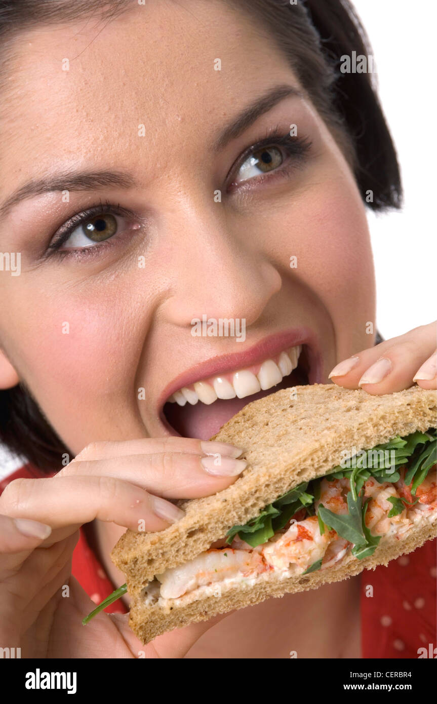 Close up of female with brunette hair biting into crayfish and salad ...
