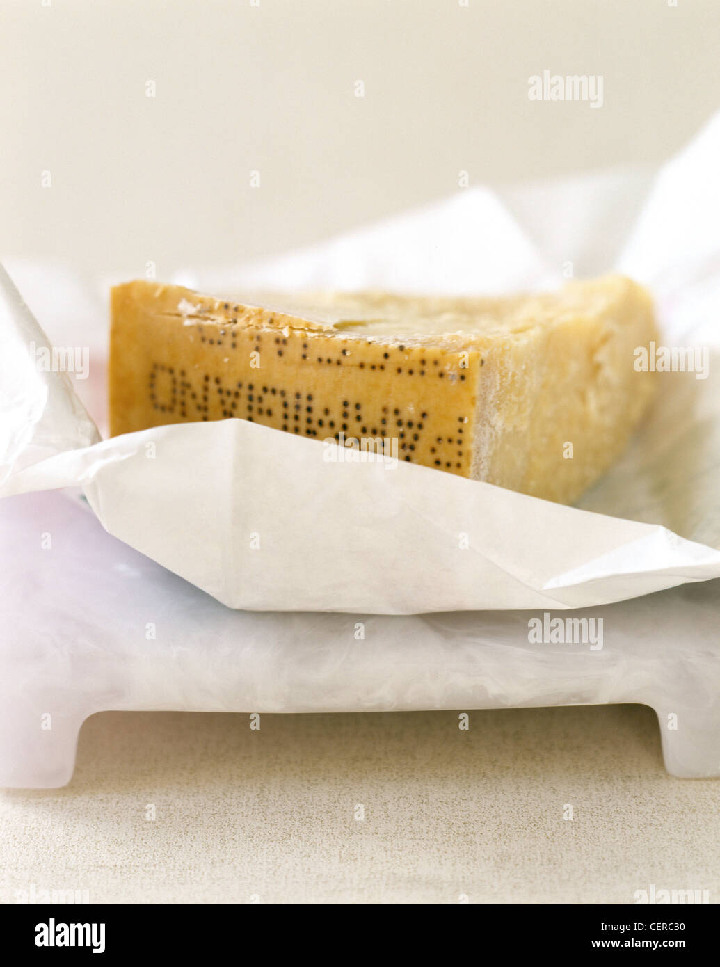 A block of parmigiano reggiano cheese in a paper wrapper on a marble ...