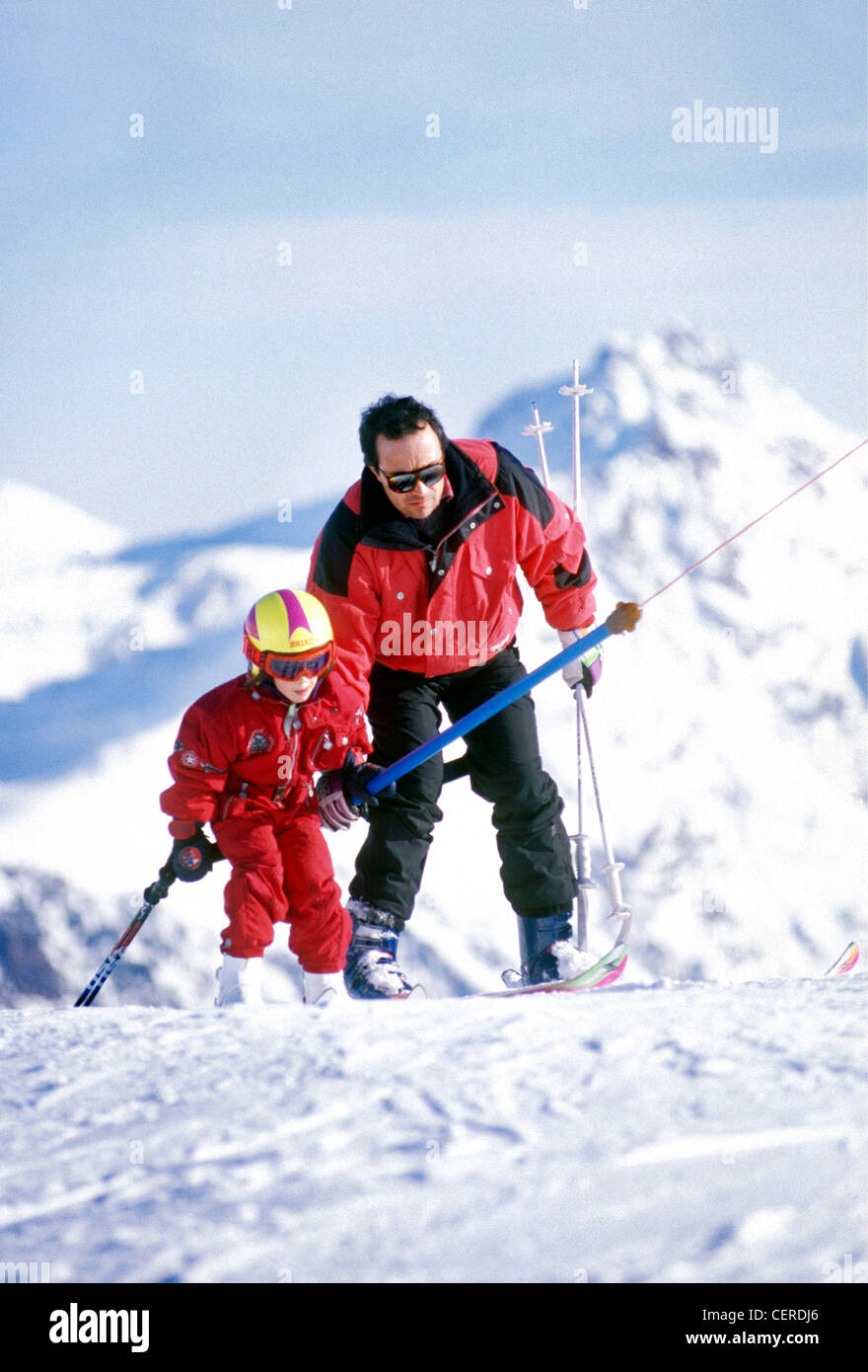 Father and child skiing in snow covered mountains, wearing red and ...