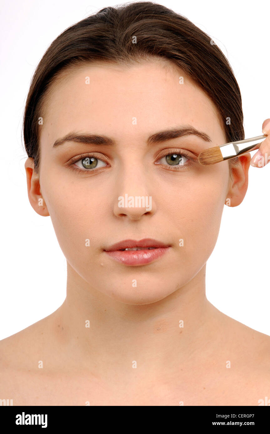 Female with brunette hair off face applying peach eyeshadow to top ...