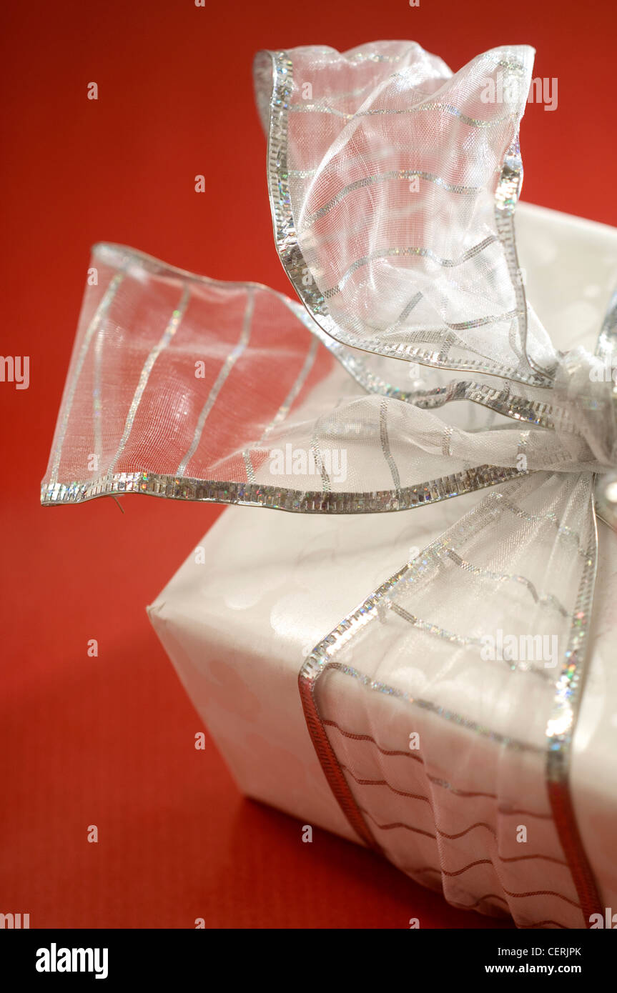 Small Christmas present wrapped with white paper with wide sheer silver ...