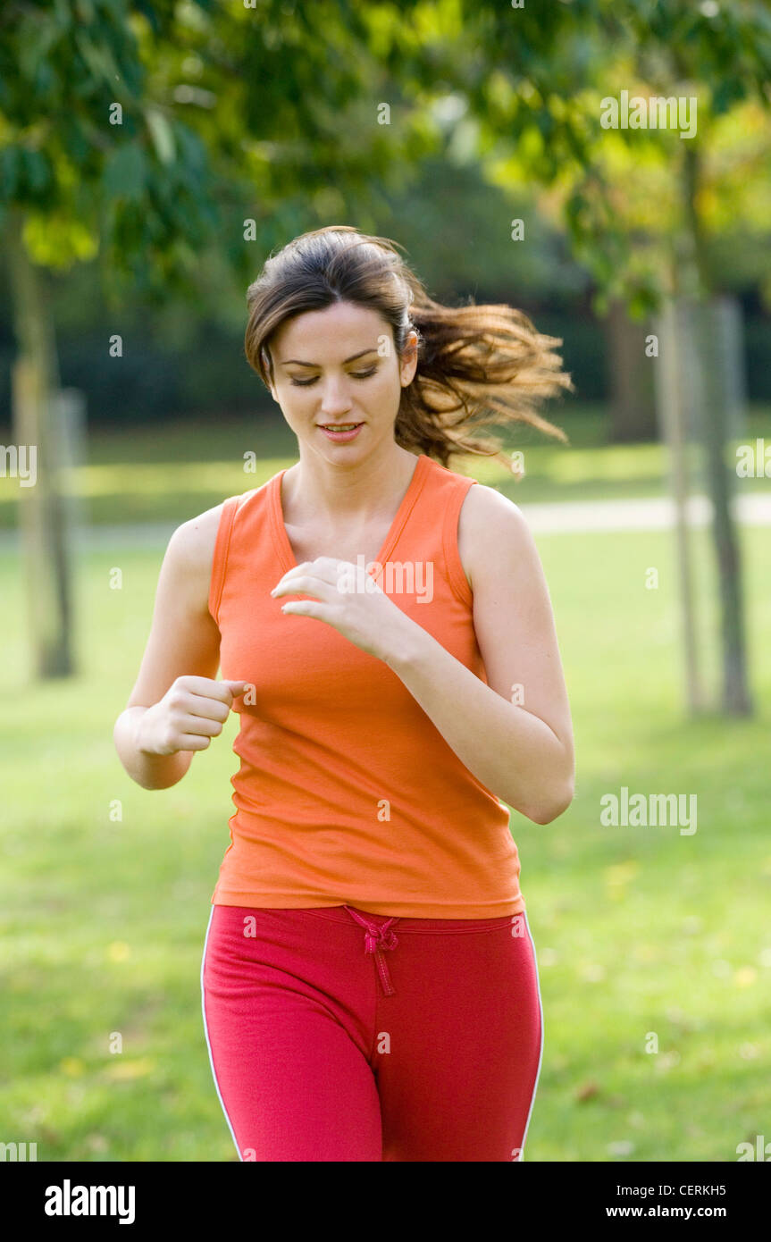 Female wearing red trousers and orange vest top running in park Stock ...