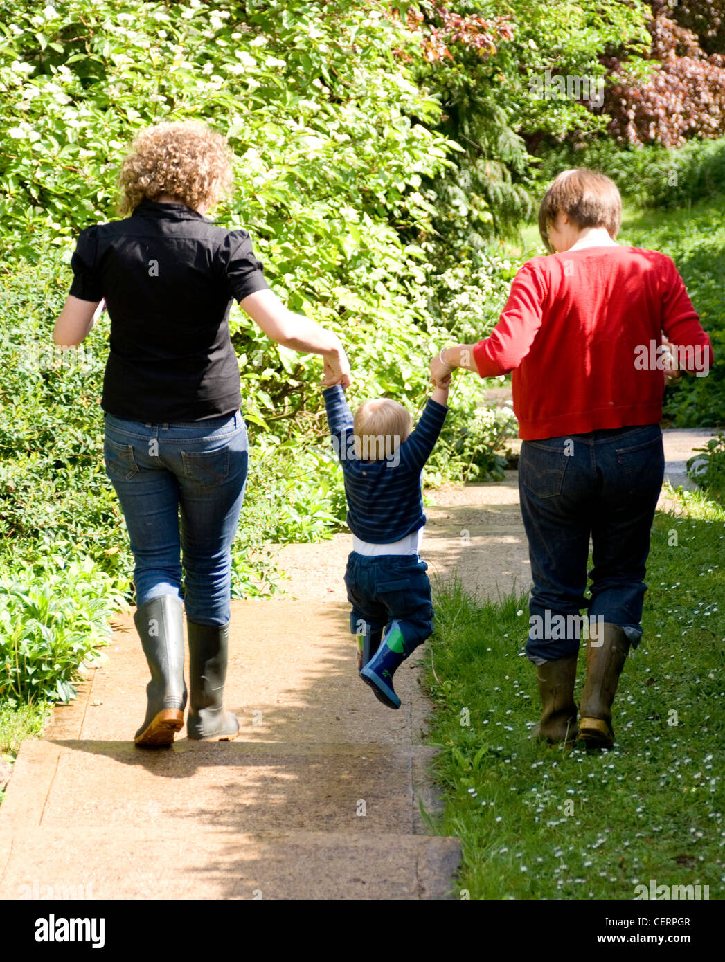 Two Females walking down path swinging child Stock Photo - Alamy