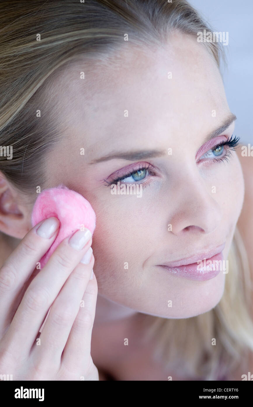 Female wearing pink eyeshadow and pale pink lipgloss rubbing her cheek ...