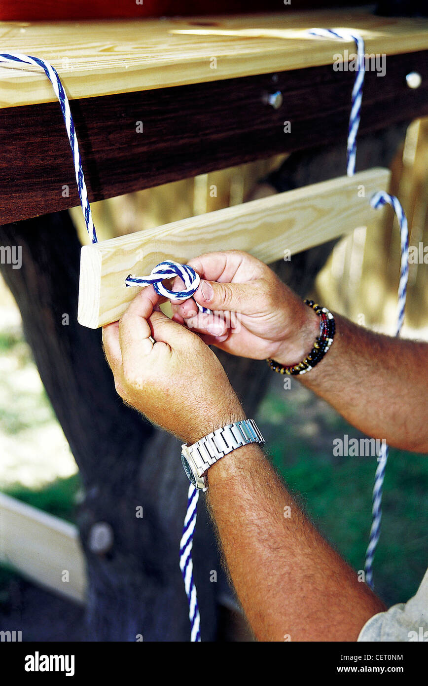 FORBuild a Tree House Step Male putting rope through the holes in wood ...