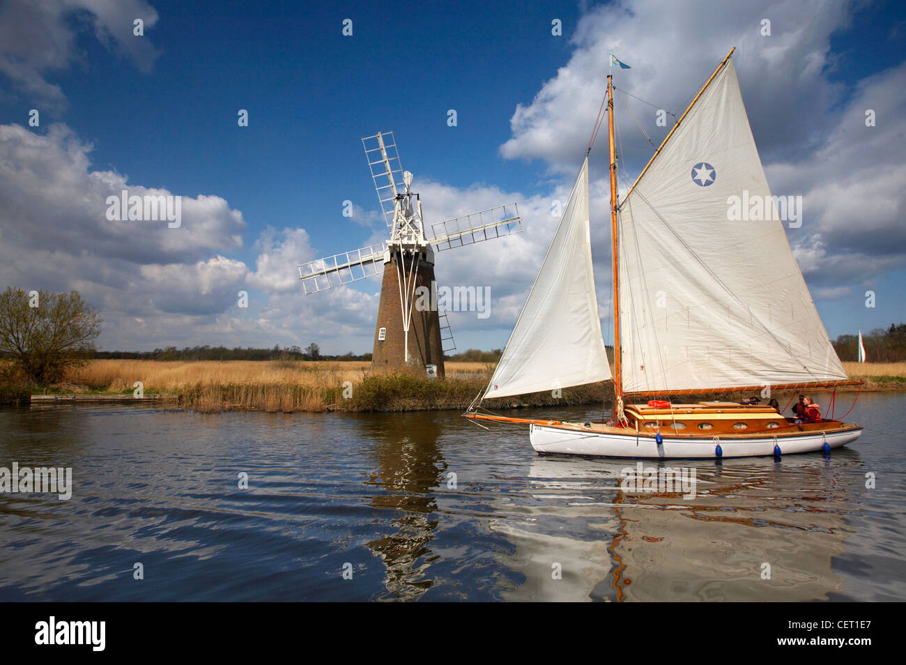A traditional wooden sailing boat sailing in front of Turf Fen windmill ...