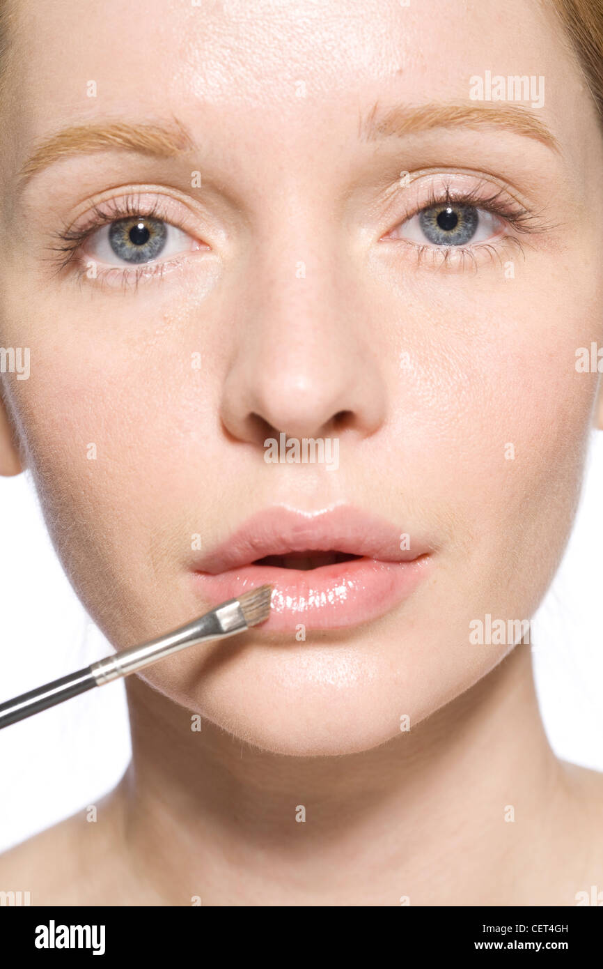 Female with fair hair off her face, applying pink lipgloss to her ...