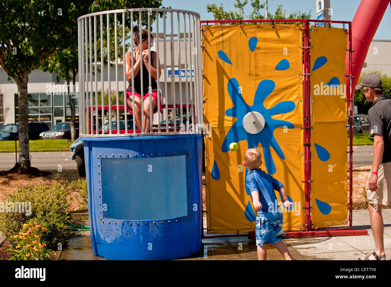 A boy threw ball at the dunk tank with a young woman sitting on it ...