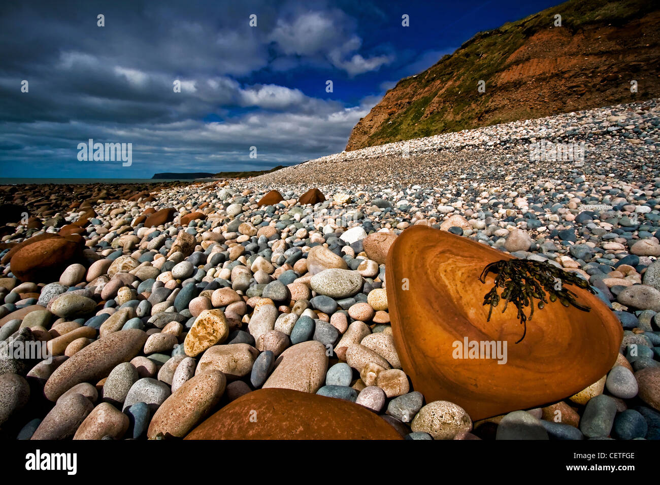 A view of red rocks on the pebble beach with cliffs in the background ...