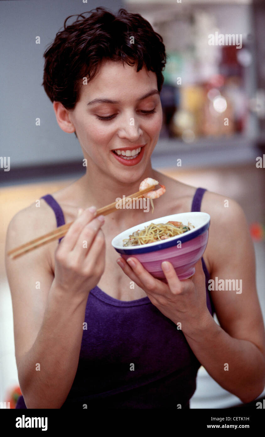 Female short brunette hair wearing blue vest top, eating prawn noodles ...