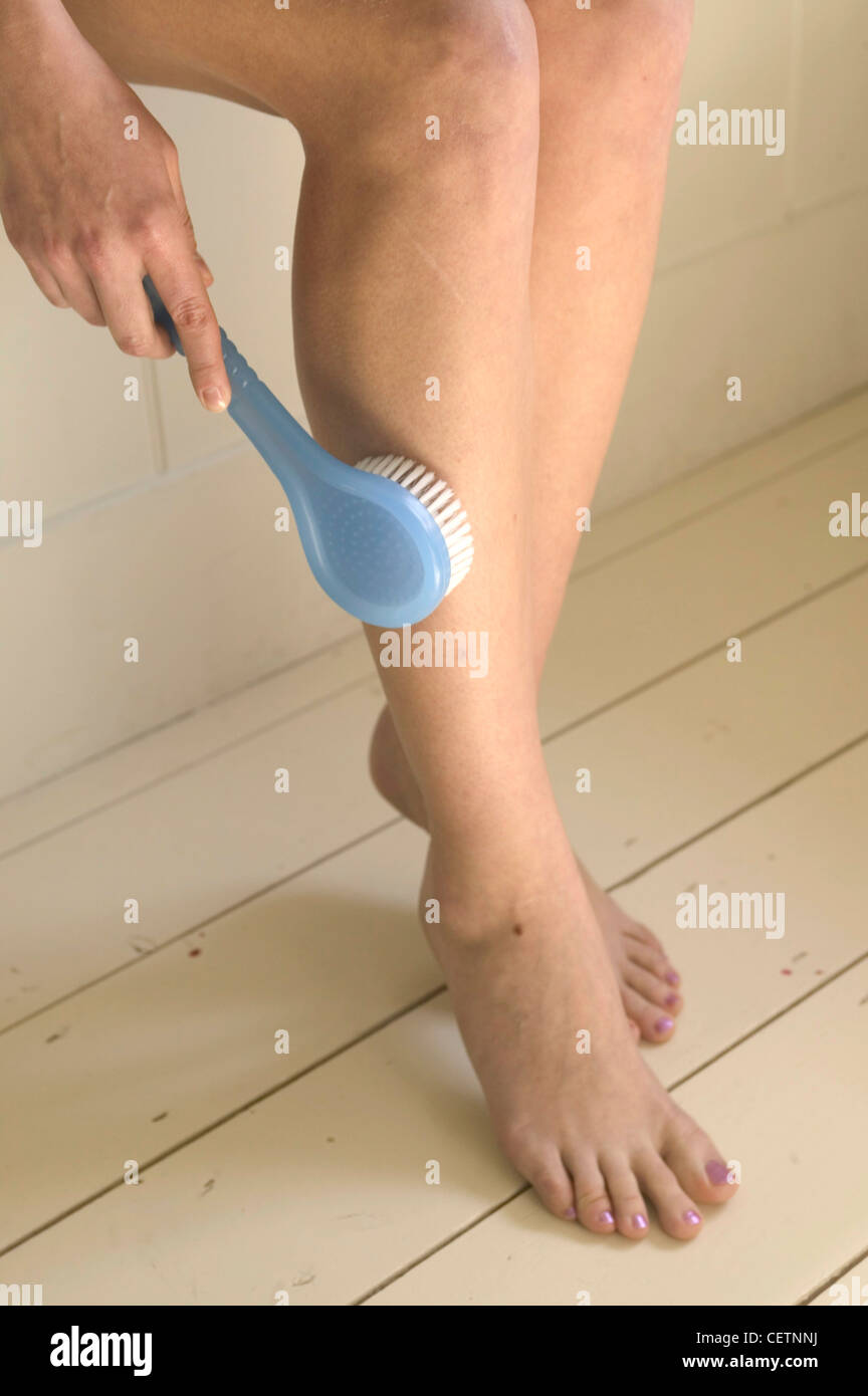 Cropped legs of female, sitting on edge of white bath exfoliating leg ...