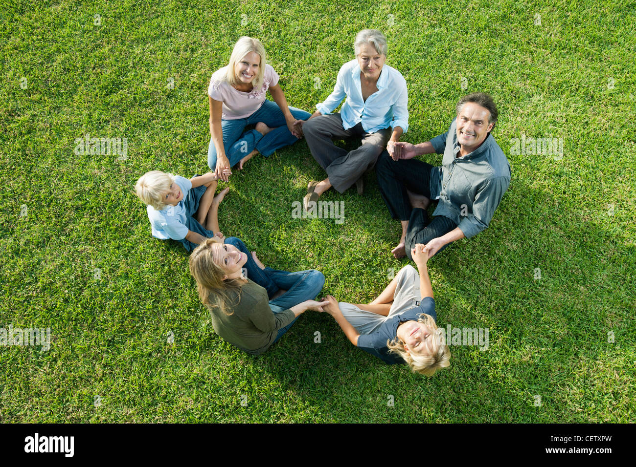 People sitting in circle on grass holding hands looking up at camera ...