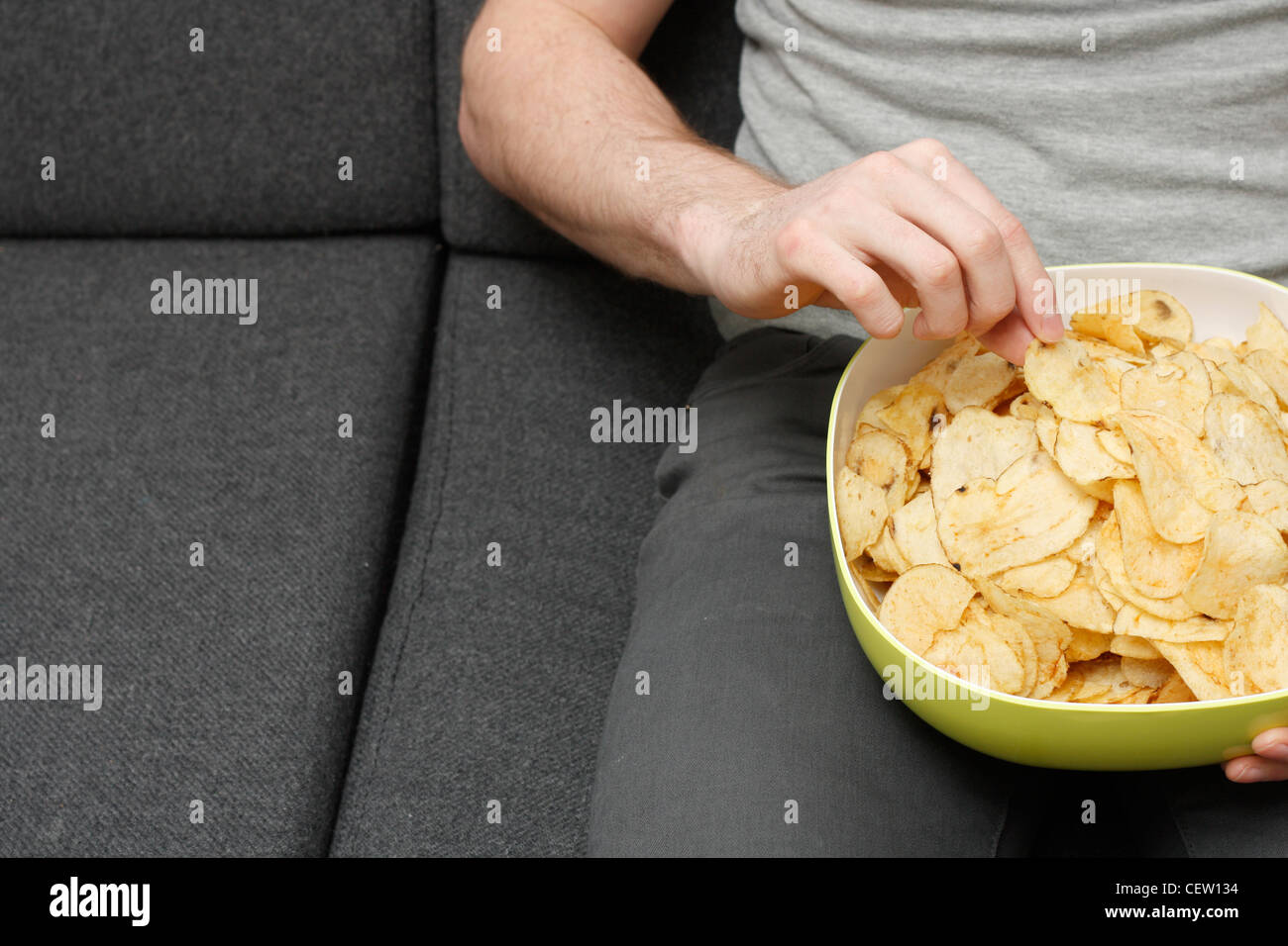 A man on a couch eating potato chips Stock Photo - Alamy