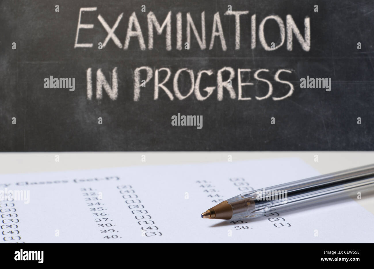 Close up on an exam paper and a pen with a blackboard in the background ...