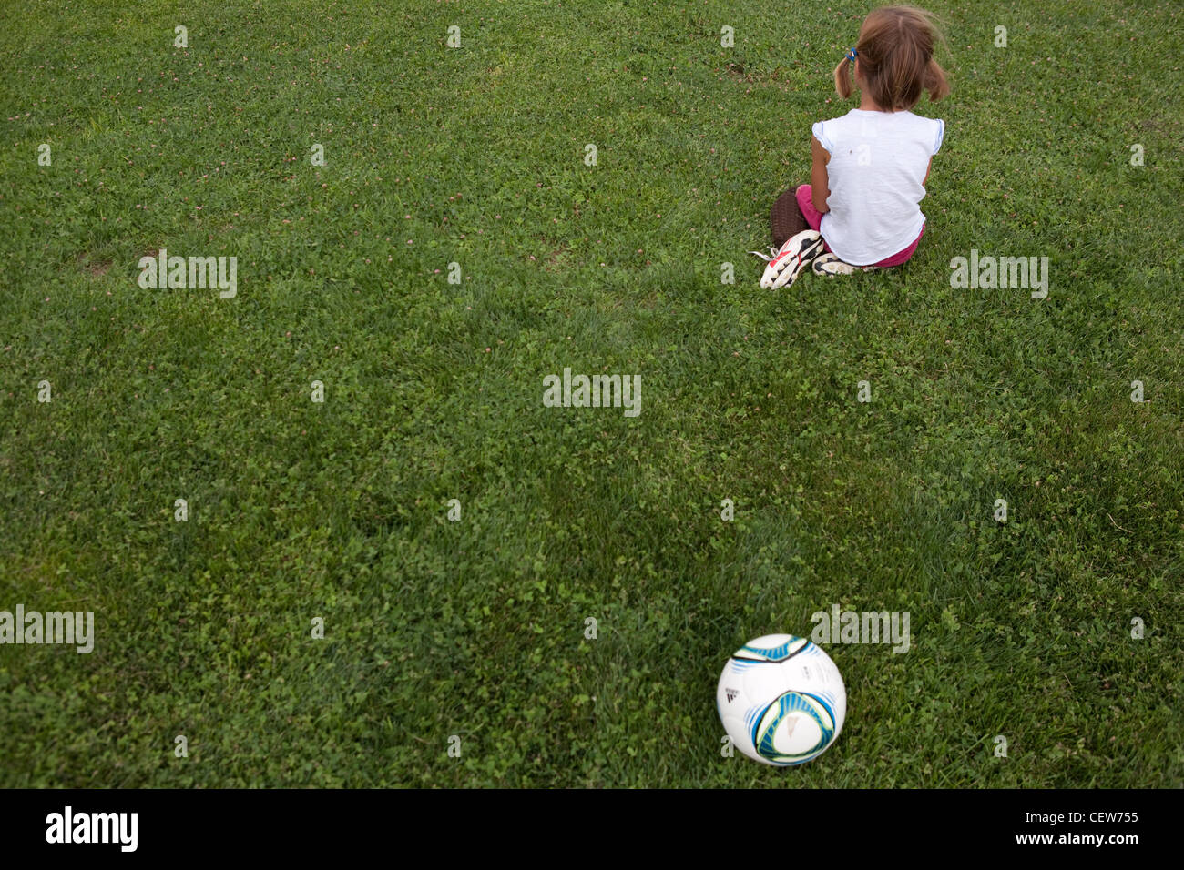 Little girl with her back turned away from a soccer ball on a grassy ...