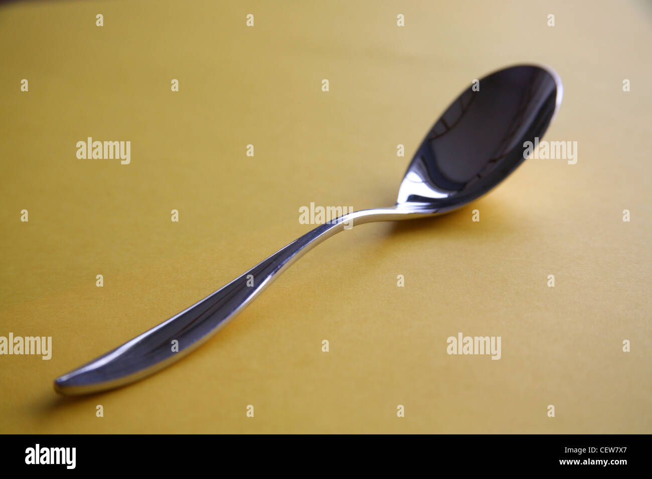 Silver spoon on yellow background Stock Photo - Alamy