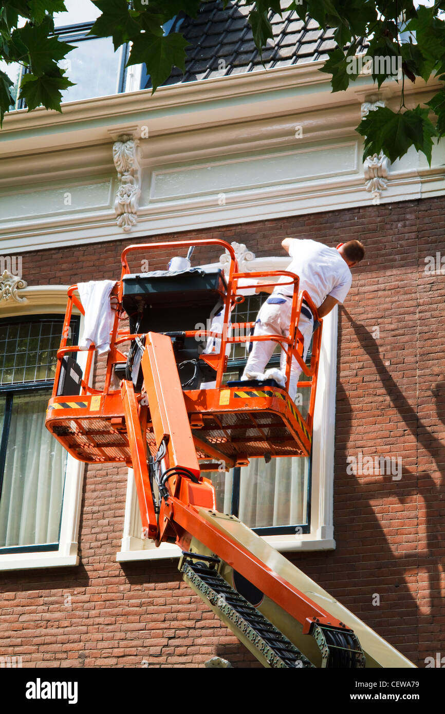 Painter on aerial access platform painting window frame Stock Photo - Alamy
