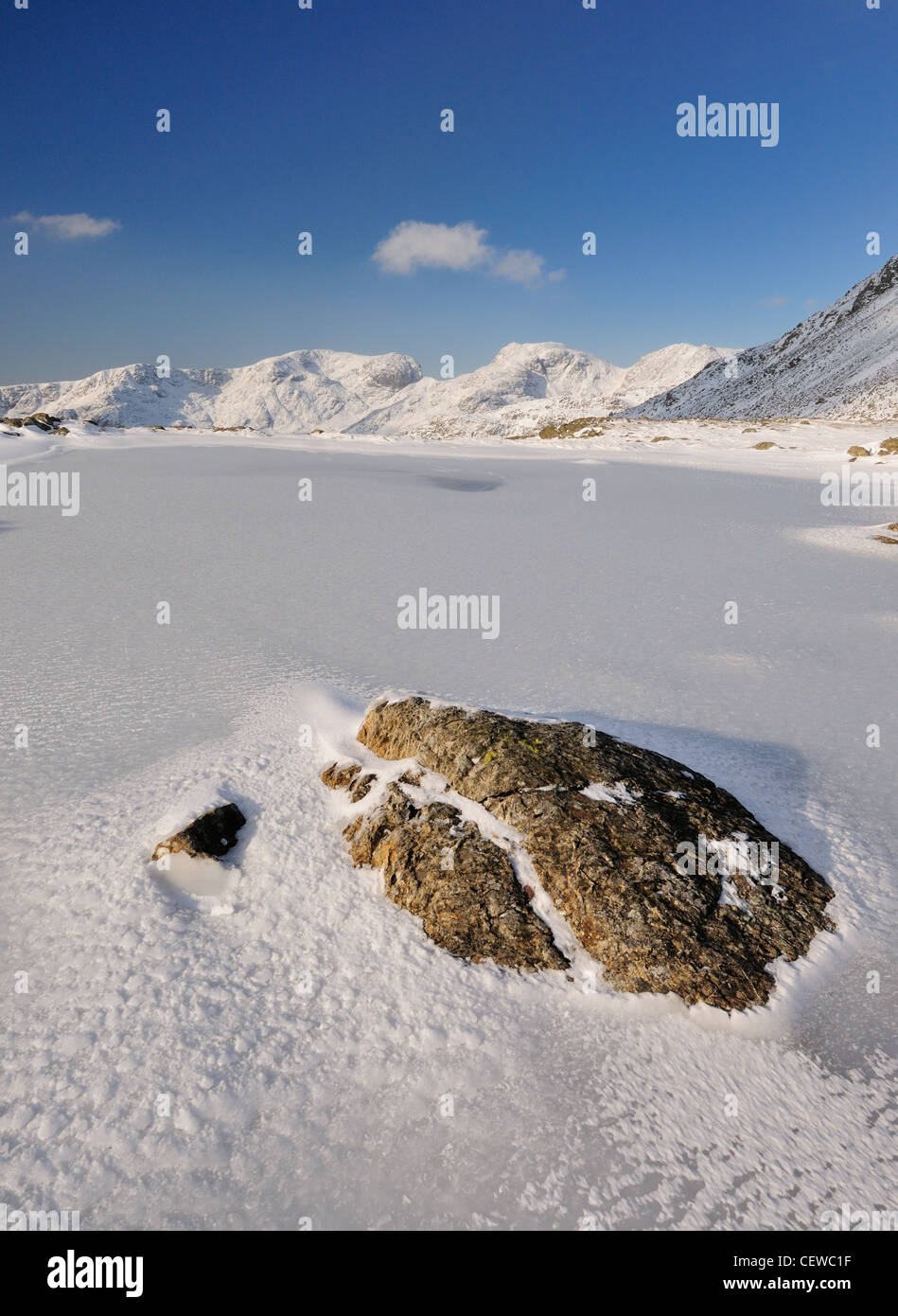 Rock and frozen Three Tarns on Bowfell with snow covered Scafell and ...