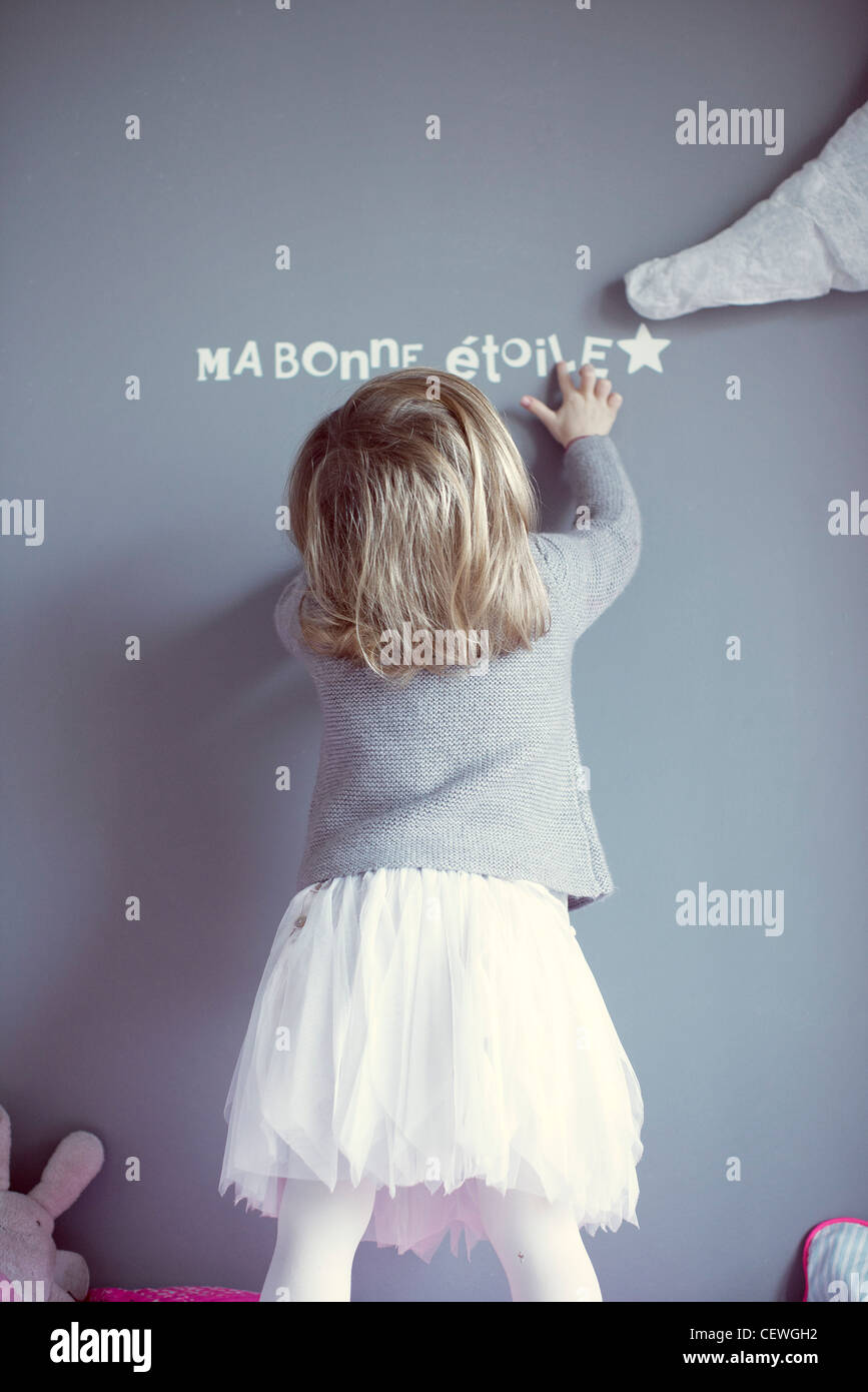 Little girl looking at words printed on wall, rear view Stock Photo - Alamy